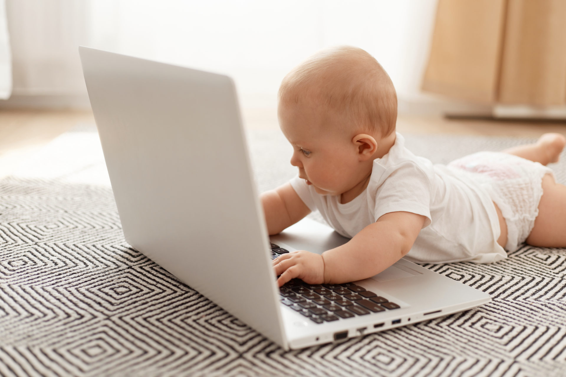 Indoor shot of charming cute child lying on tummy and watching cartoons ...